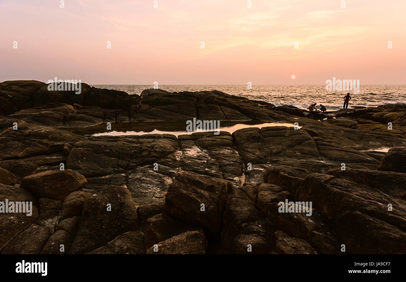 Locals shell fish for mollusc on Chera rock at dusk with view of ...