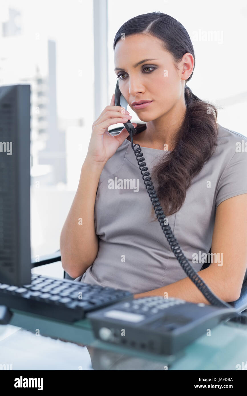 Serious secretary answering land line in her office looking at computer ...