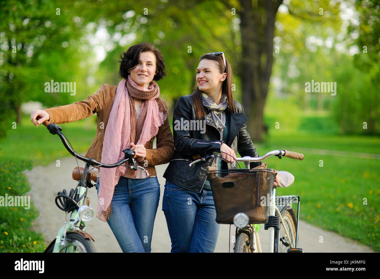 Two charming young women on bicycle walk in the spring park ...