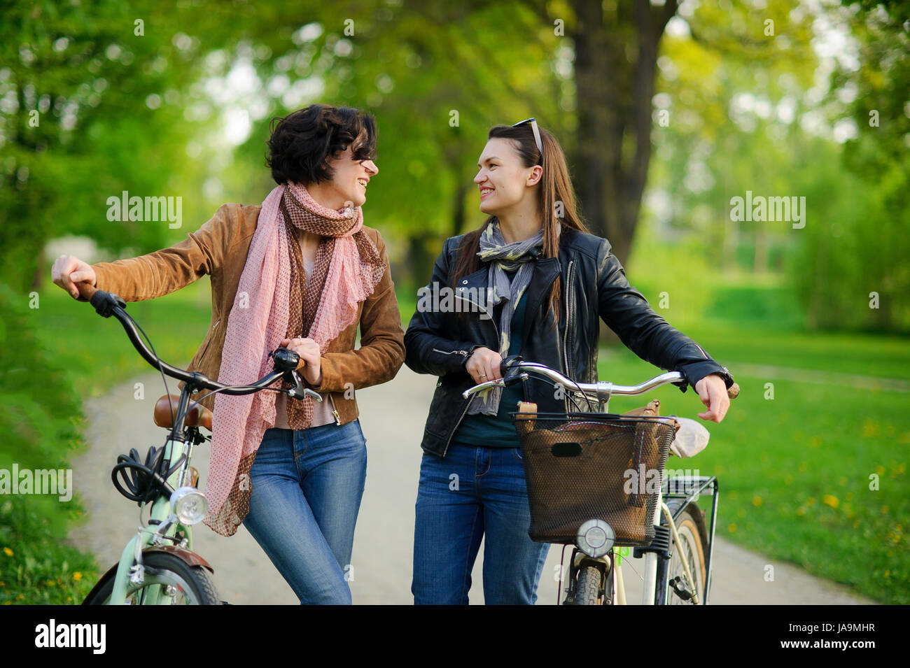 Two charming young women on bicycle walk in the spring park ...