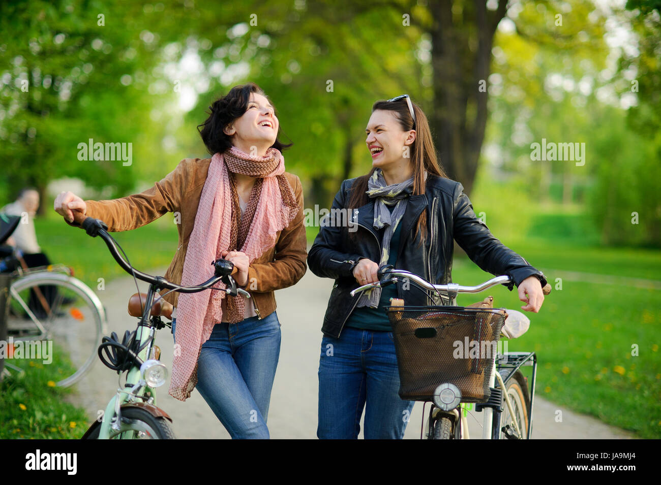 Two charming young women on bicycle walk in the spring park ...