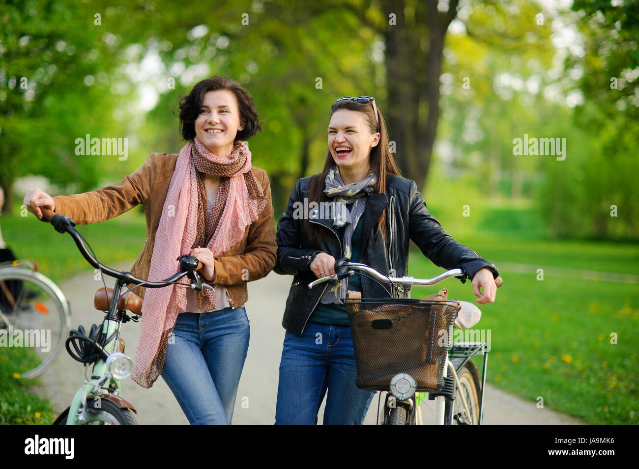 Two charming young women on bicycle walk in the spring park ...