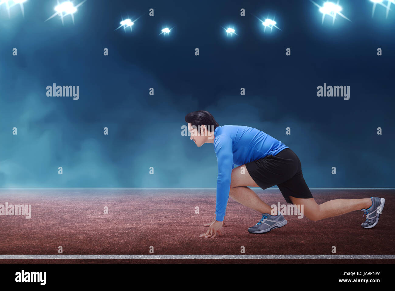 Young asian runner man kneeling ready in start position on race track ...