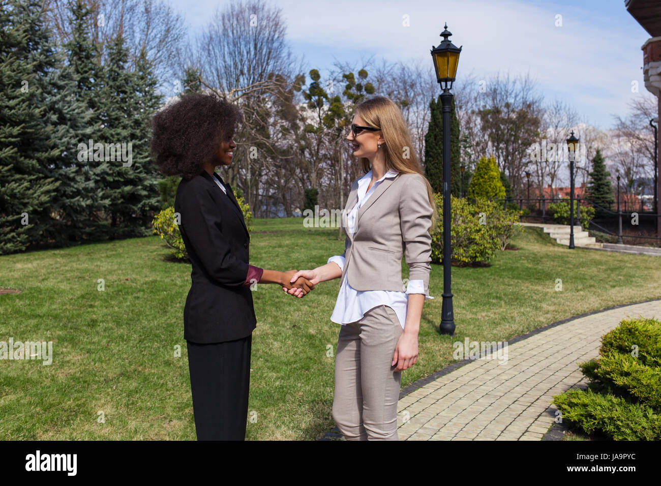 Black woman shaking hands with blonde. Businesswoman standing outside ...
