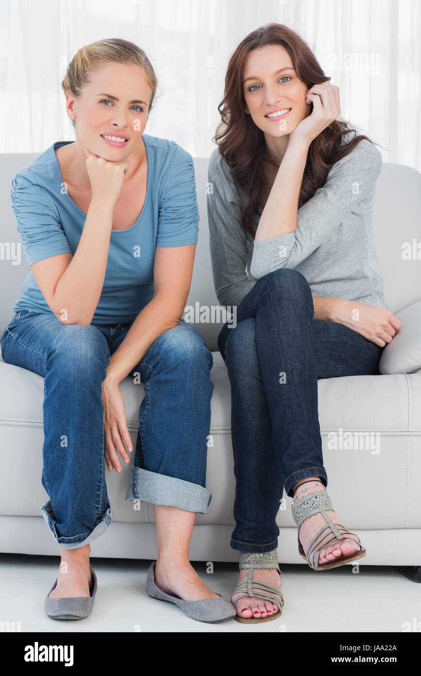 Two relaxed women posing while sitting on the couch and looking at ...