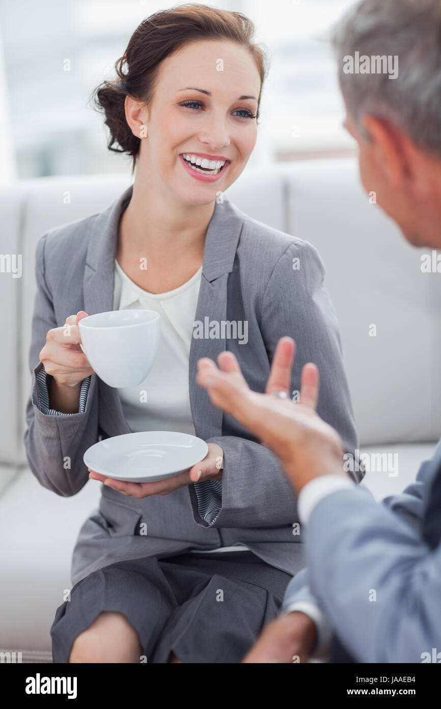 Cheerful businesswoman having coffee with her workmate in bright office ...