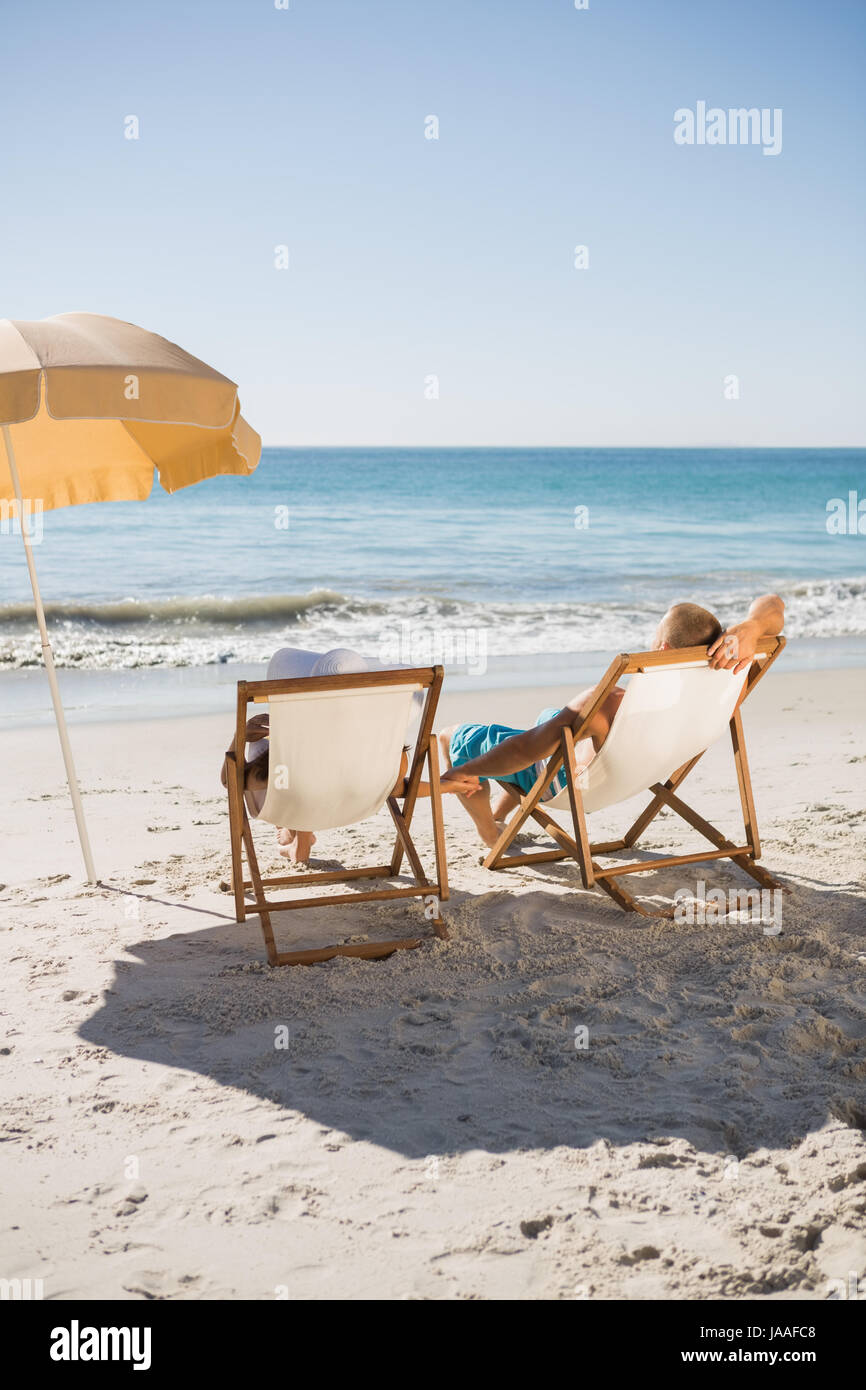 Happy couple on the beach sunbathing on their deck chairs Stock Photo ...