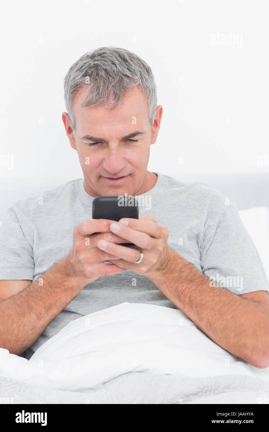 Smiling grey haired man sending a text in bed in bedroom at home Stock ...