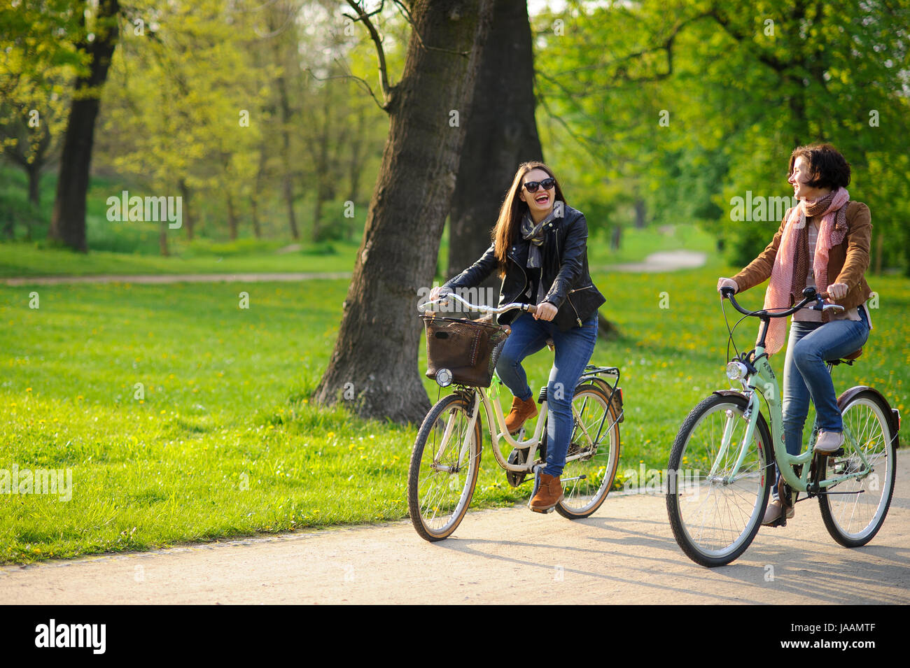Two young women ride bikes in the spring park. Gentle spring greens ...