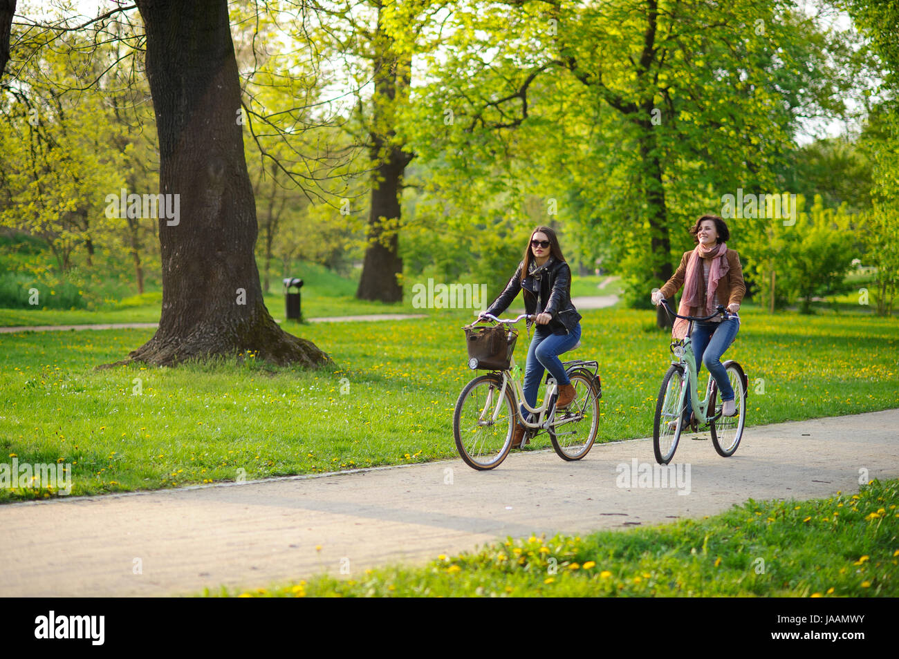 Two young women ride bikes in the spring park. Gentle spring greens ...