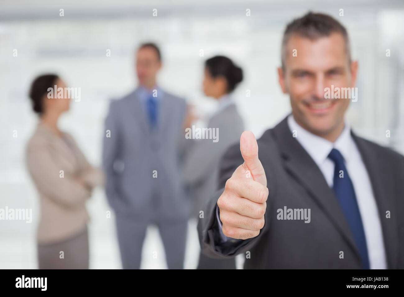 Smiling manager showing thumb up with employees in background in bright ...