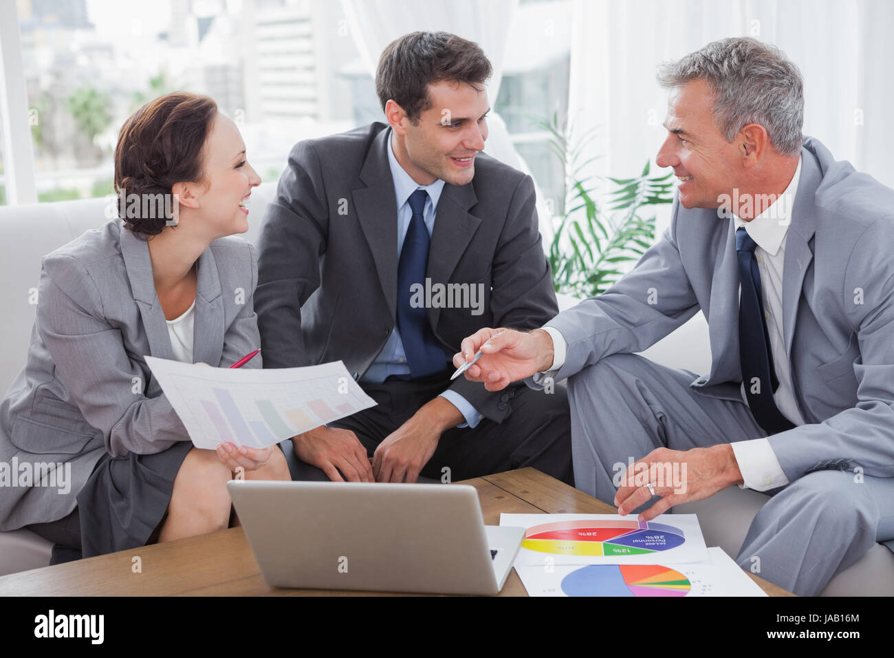 Cheerful business people analyzing financial graphs of their company in ... Cheerful business people analyzing financial graphs of their company in ...