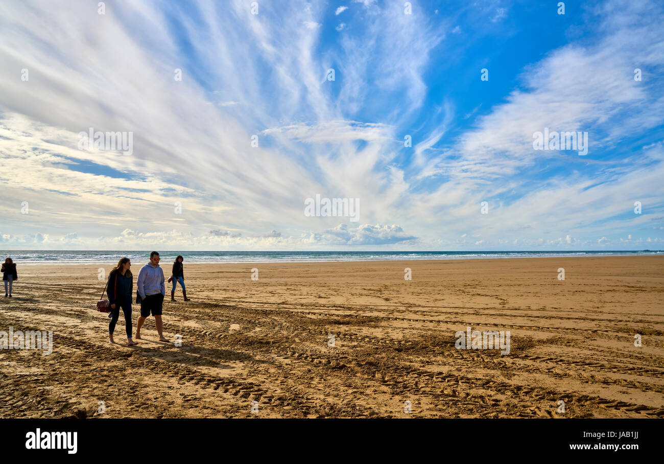 People walking on the beach underneath a big blue sky with high white ...