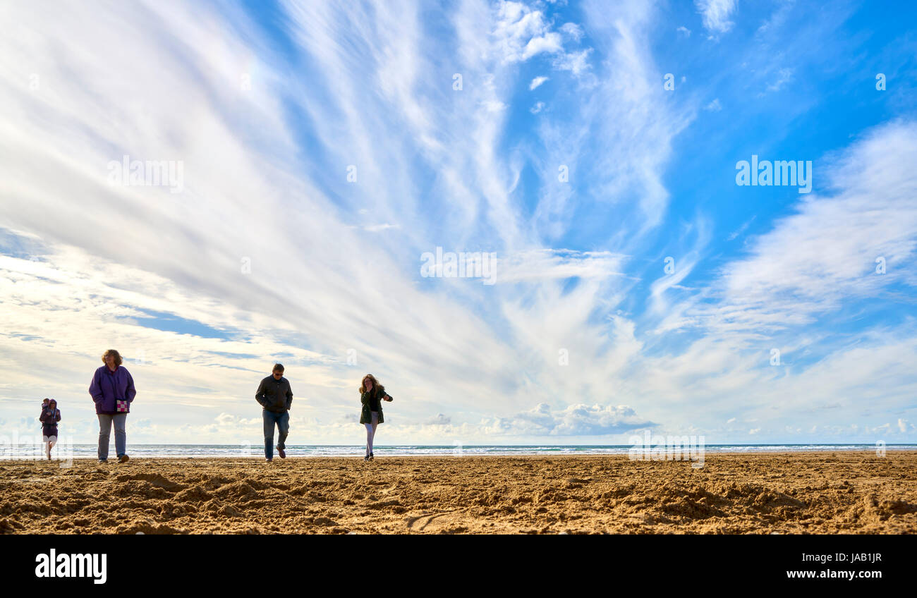 People walking on the beach underneath a big blue sky with high white ...