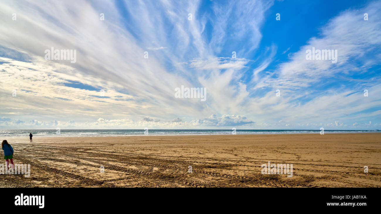 People walking on the beach underneath a big blue sky with high white ...