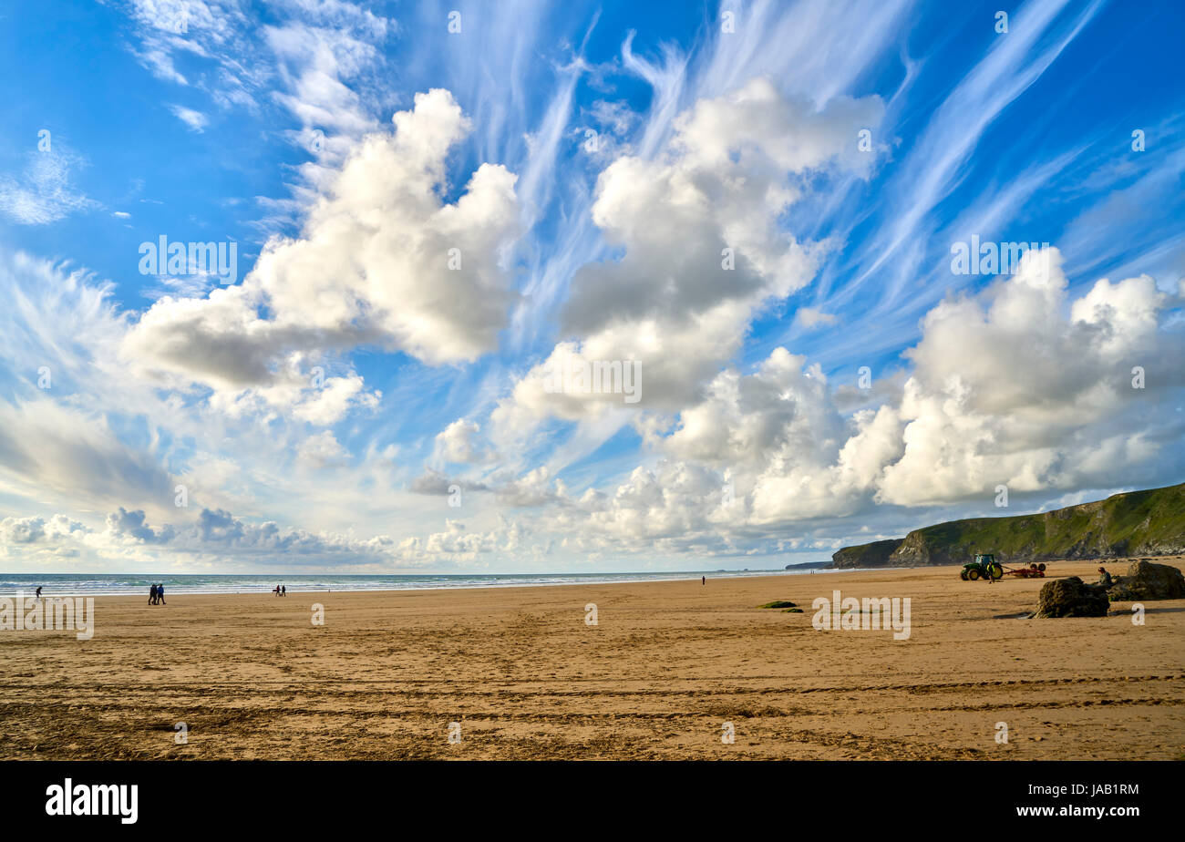 People walking on the beach underneath a big blue sky with high white ...