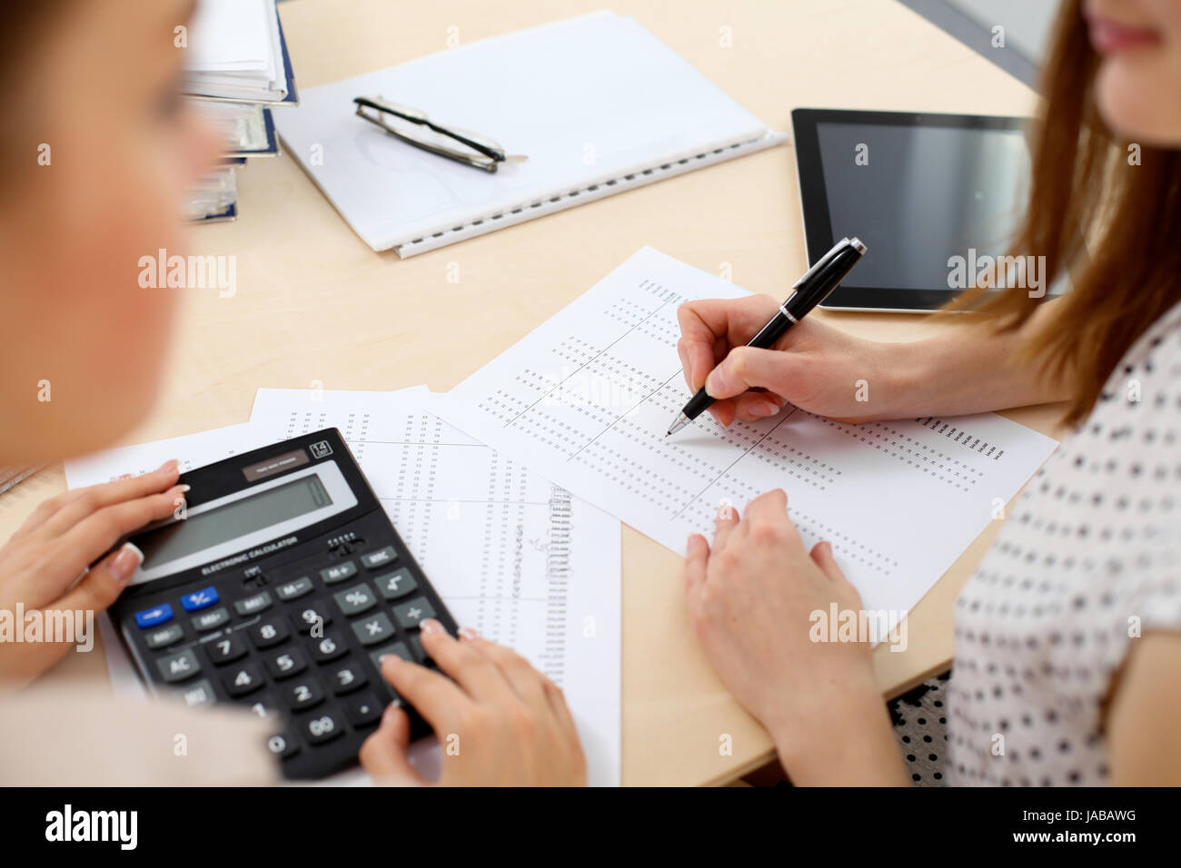 Two female accountants counting on calculator income for tax form ...