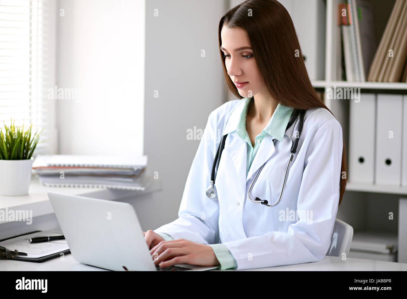 Female doctor brunette sitting at the table near the window in hospital ...