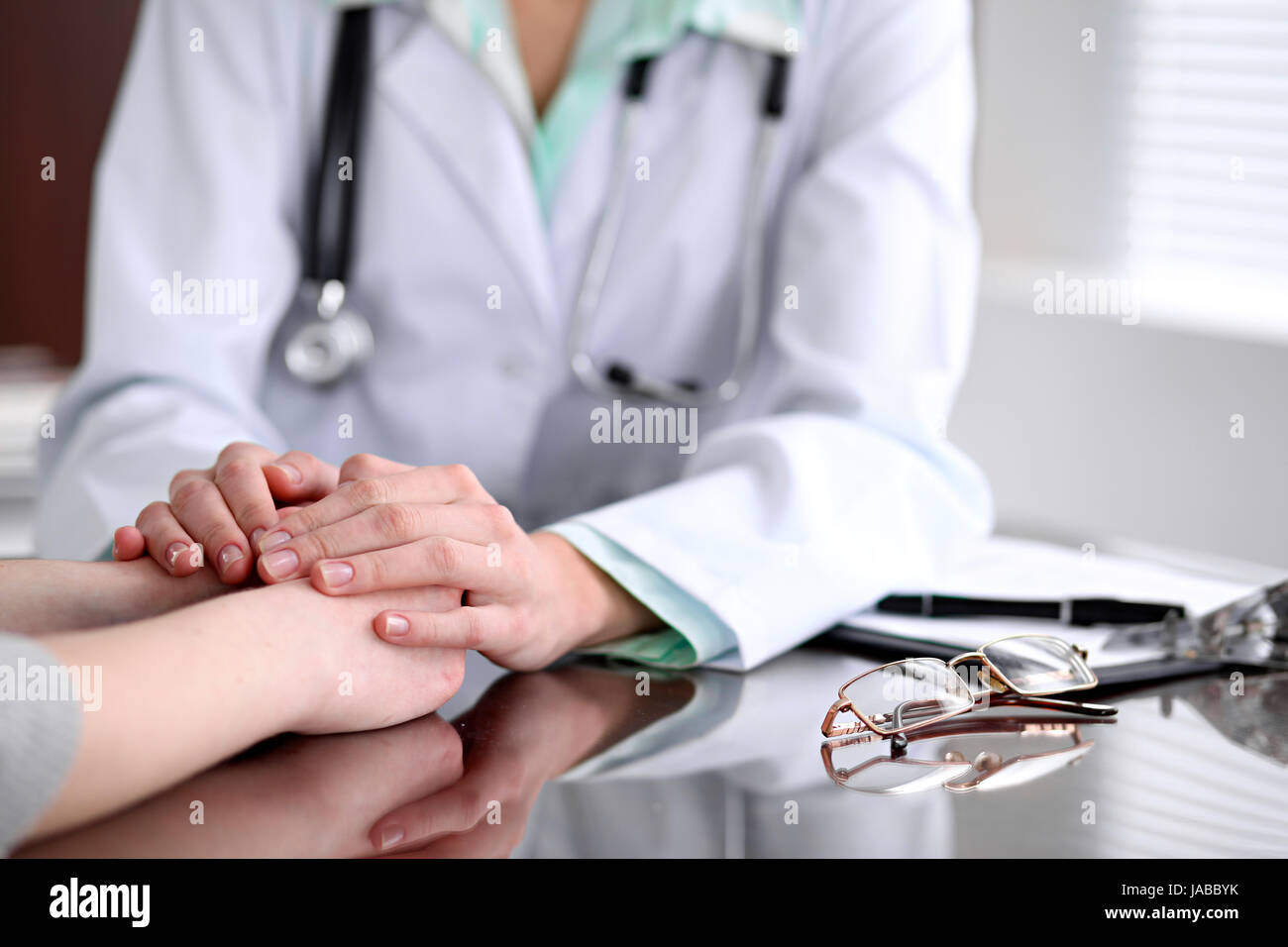 Friendly female doctor hands holding patient hand sitting at the desk ...