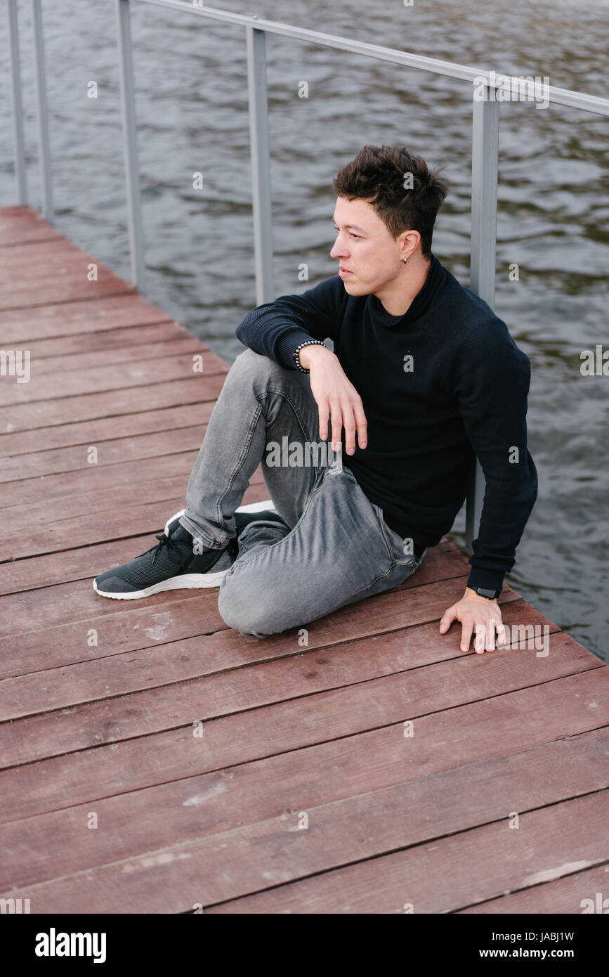 Young man sitting on a wooden pier Stock Photo - Alamy