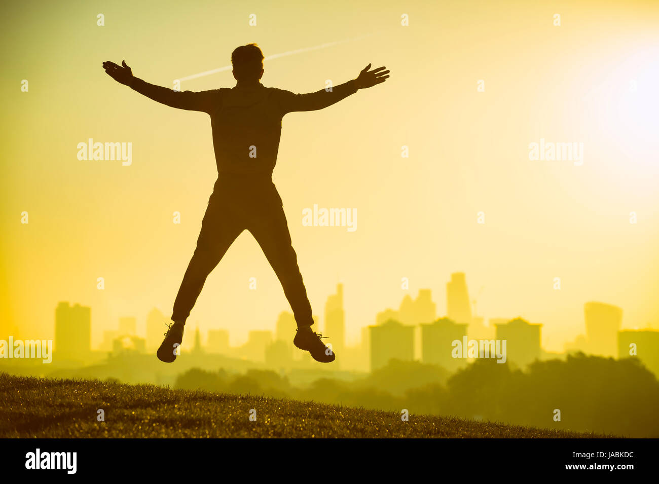 Silhouette of a man star-jumping with hands in the air looking out at ...
