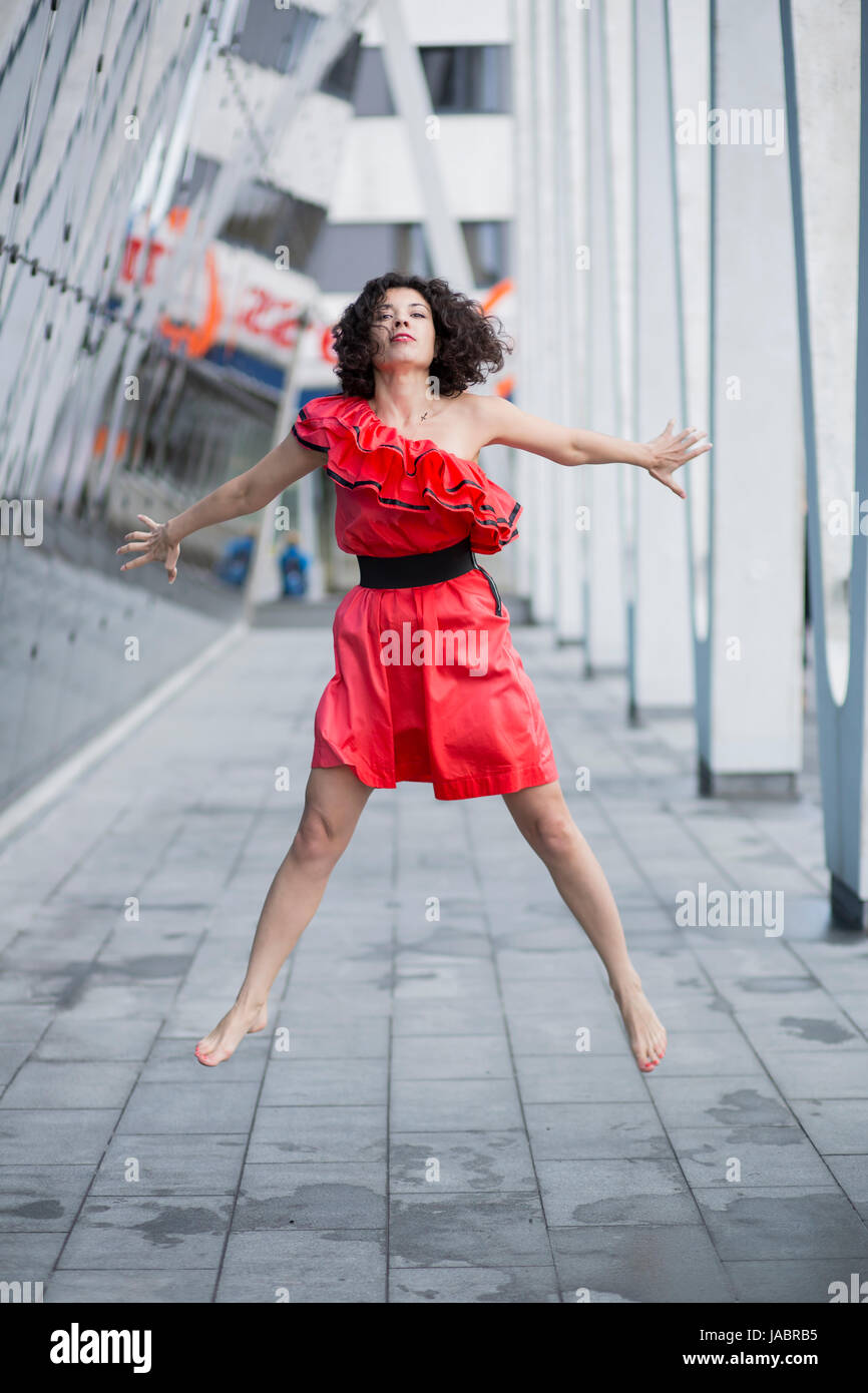 Woman in red dress jump both hands behind Stock Photo - Alamy