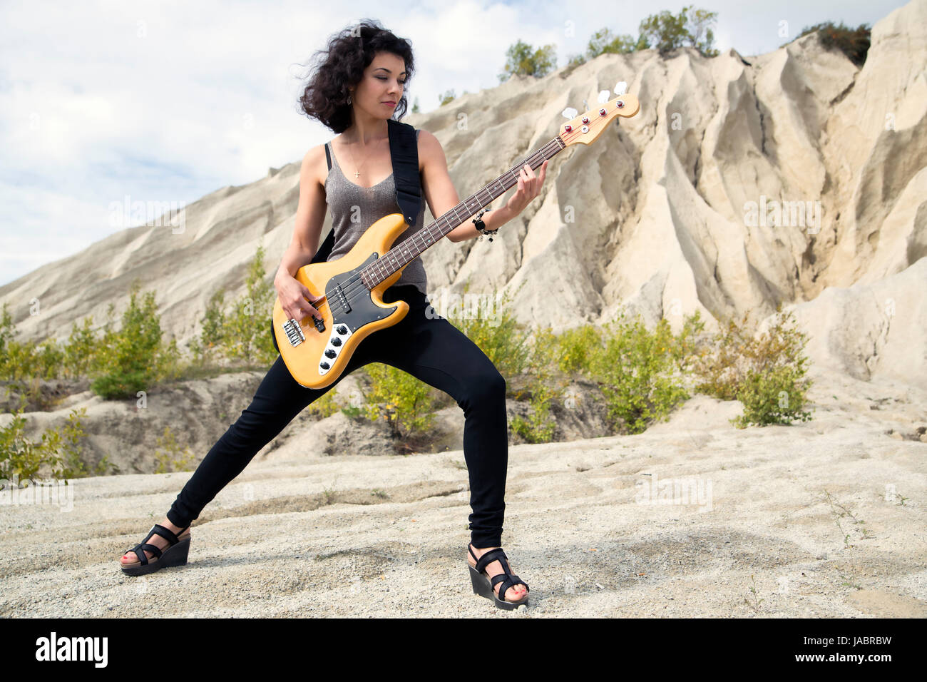 Woman on sandy background with yellow bass guitar Stock Photo - Alamy