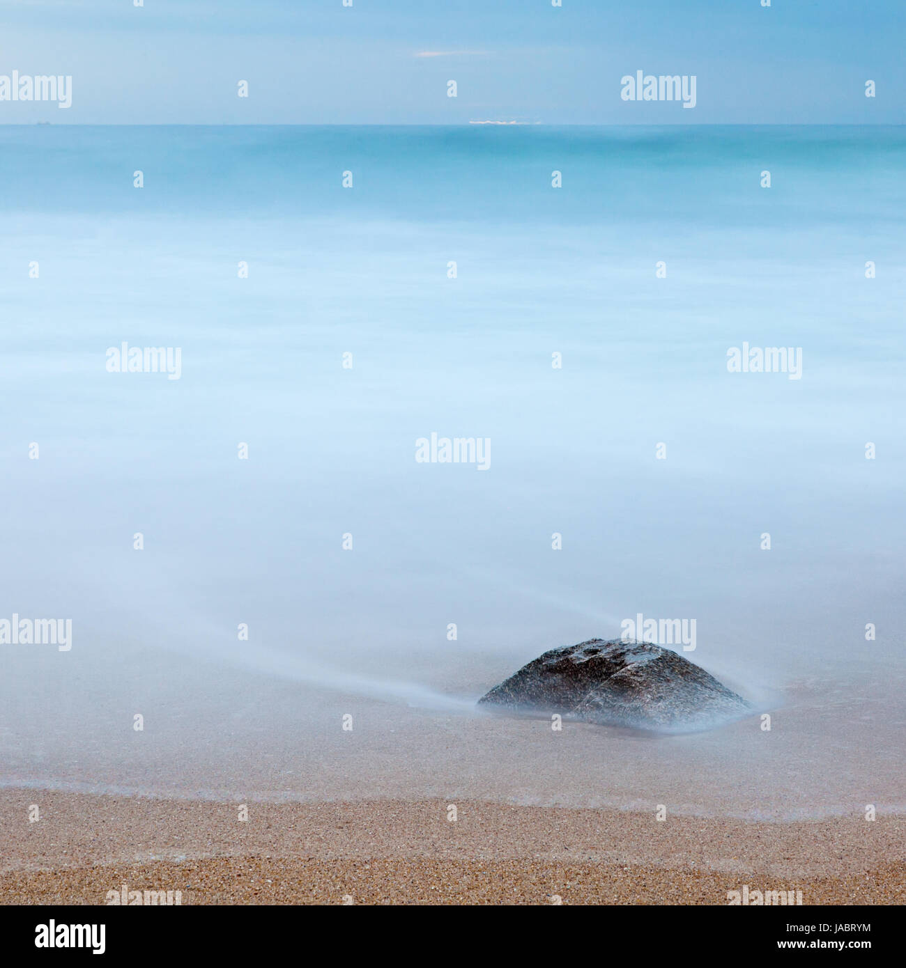 Photo of a rock on a beach, buried in the sand and covered by the ocean ...