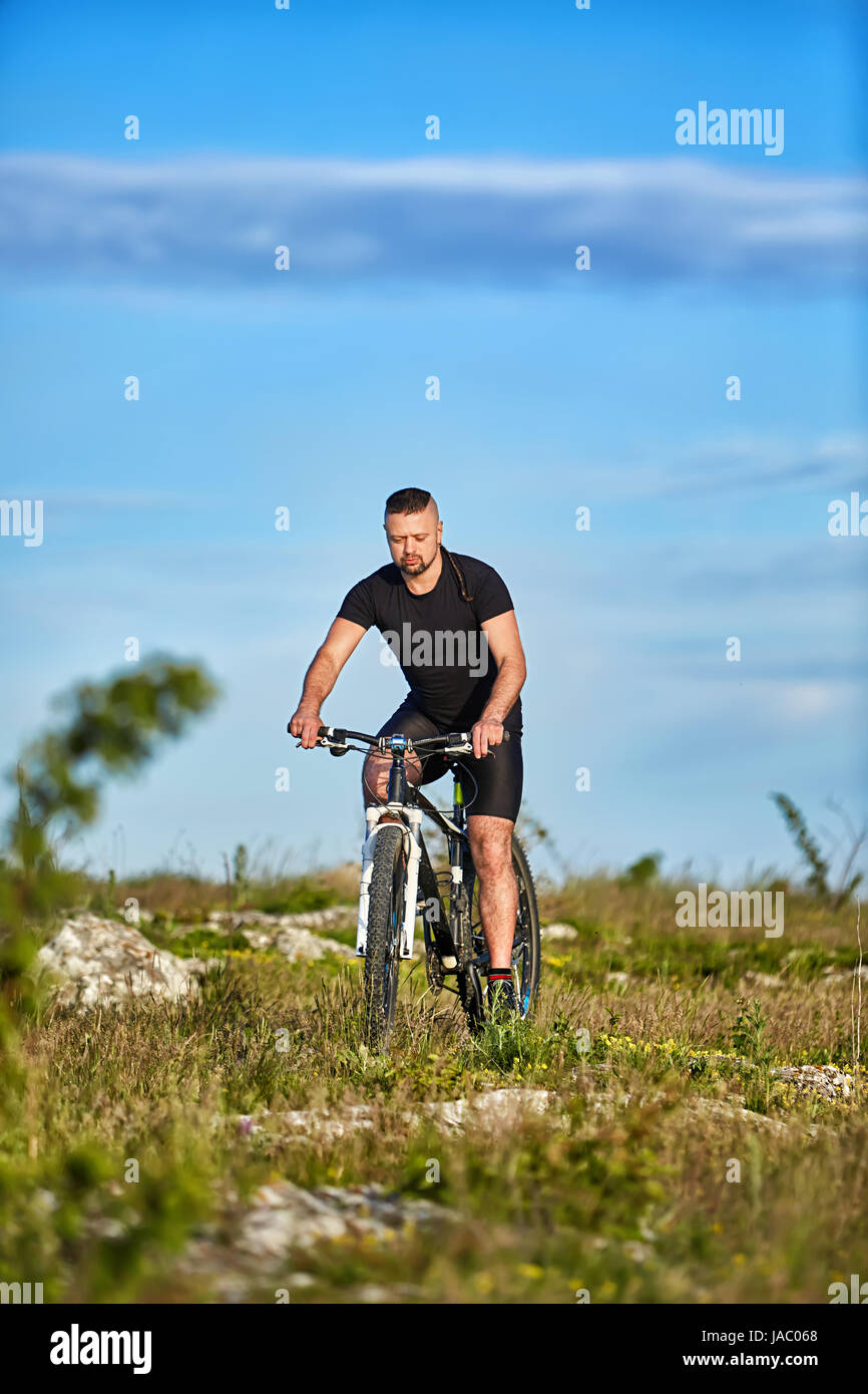 Attractive sportsman riding bike on rocky trail against sky with clouds ...