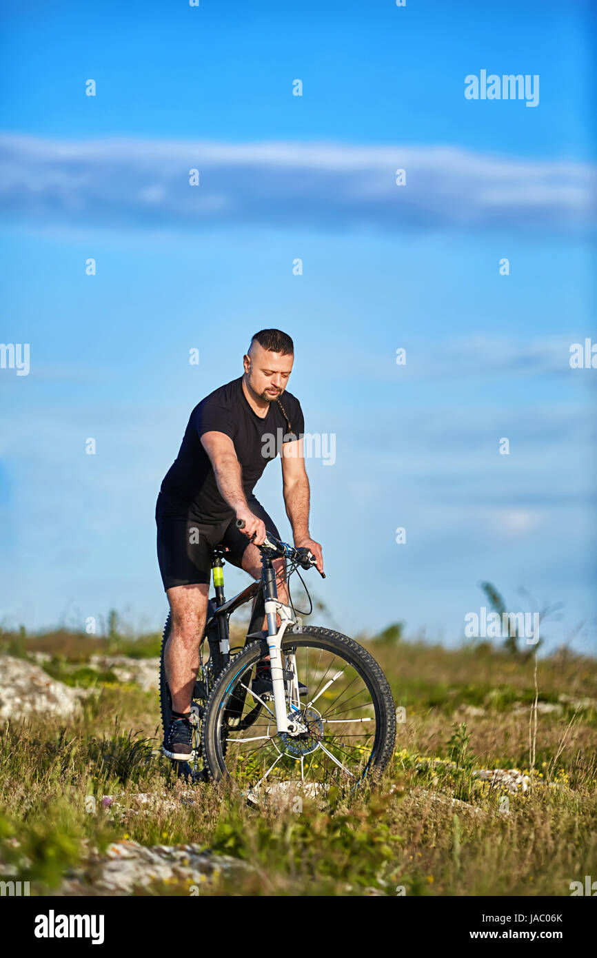 Attractive sportsman riding bike on rocky trail against sky with clouds ...