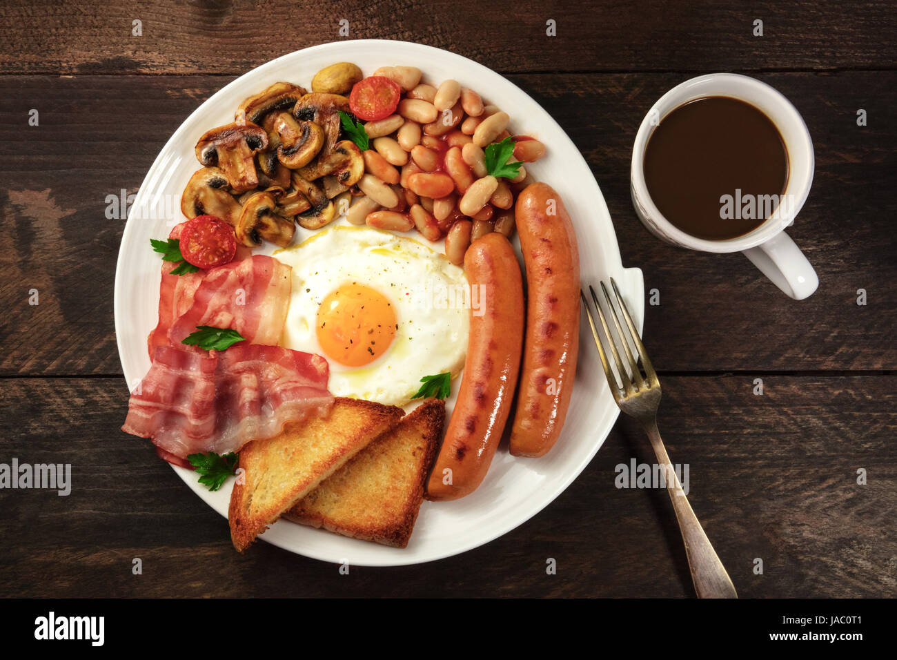 An overhead photo of a plate of English breakfast on a dark rustic ...