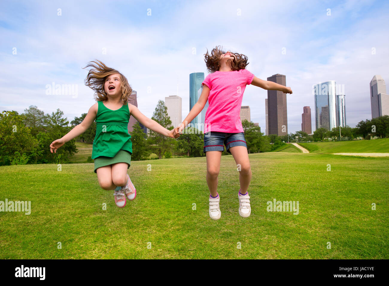 Two sister girls friends jumping happy holding hand in urban modern ...
