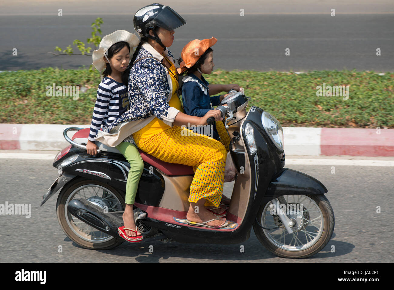 A mother rides on a motorbike with her children in Mandalay, Myanmar ...