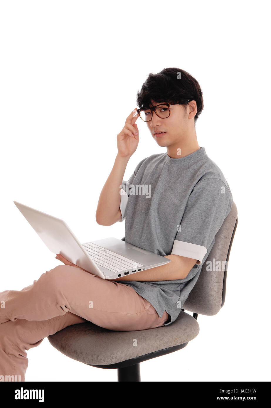 A young Asian man sitting on a chair and working on his laptop, with ...