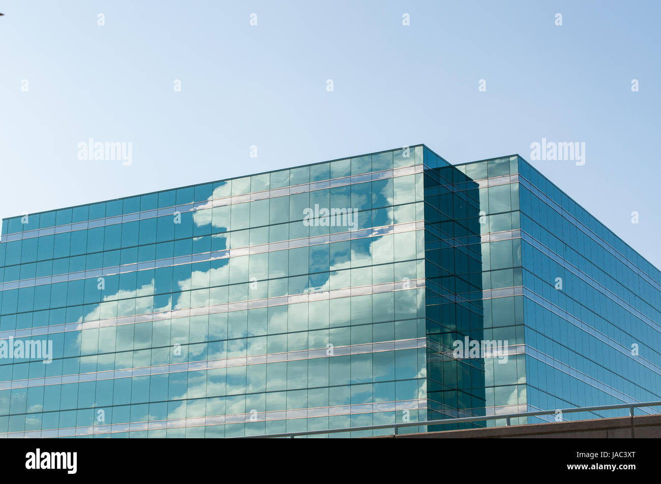 A modern reflective office building reflects the white clouds in a blue ...