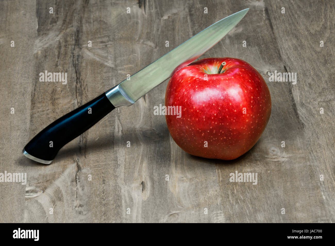 The knife cuts a red apple lying on a wooden surface Stock Photo - Alamy