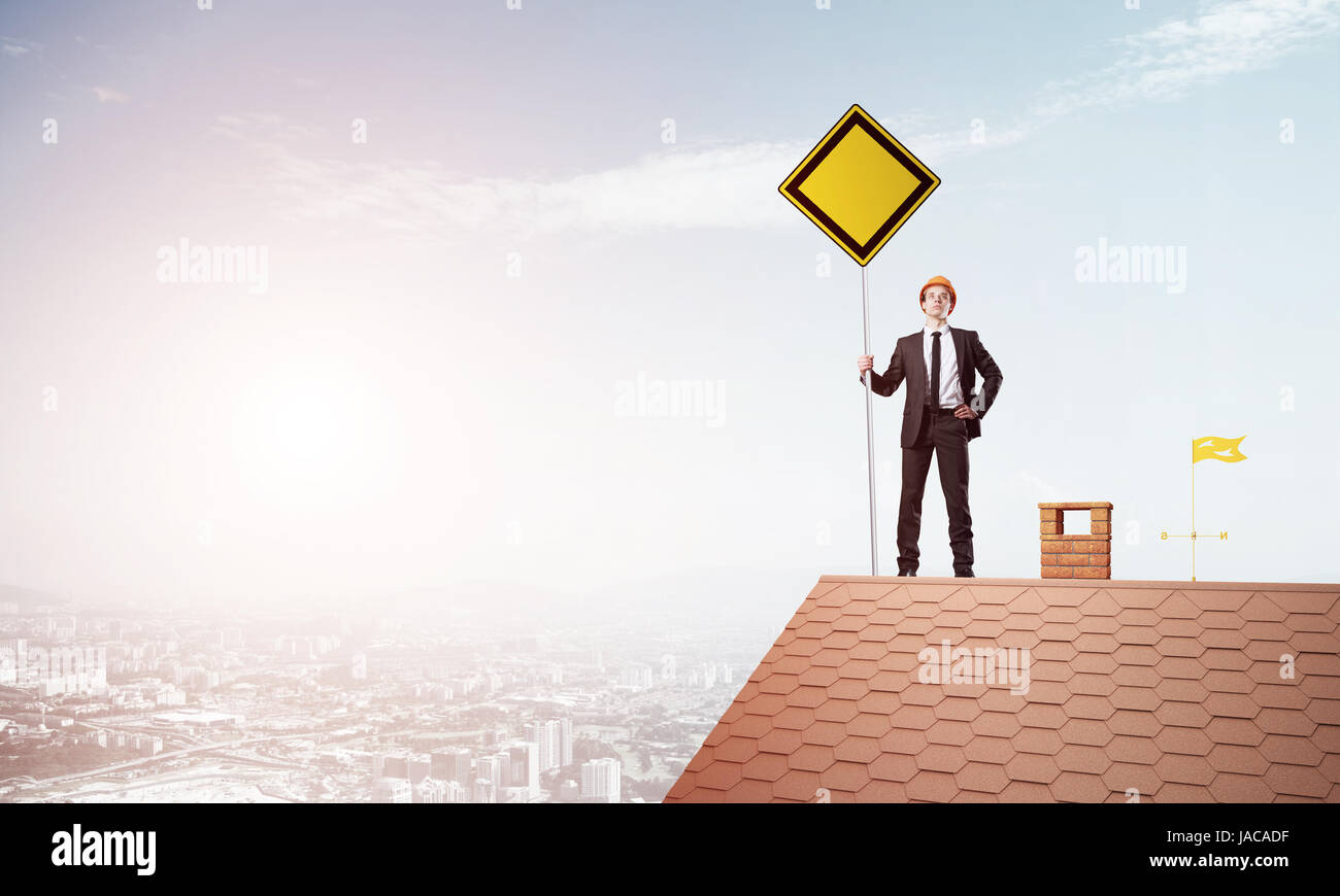 Young businessman on house brick roof holding yellow signboard and ...