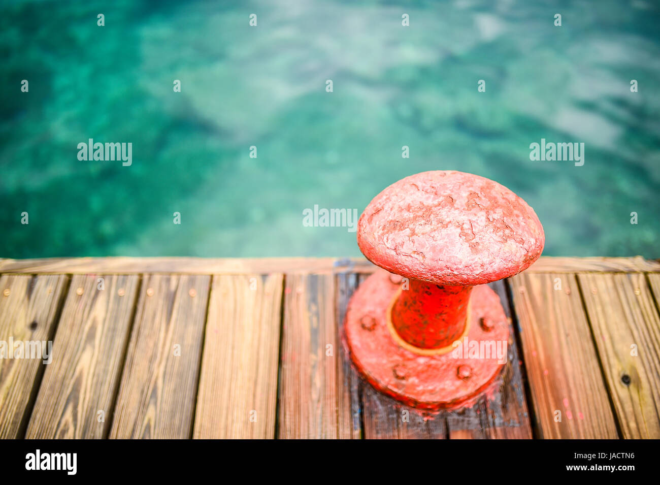 Red bollard with a mooring rope on the pier at the port and sea water ...