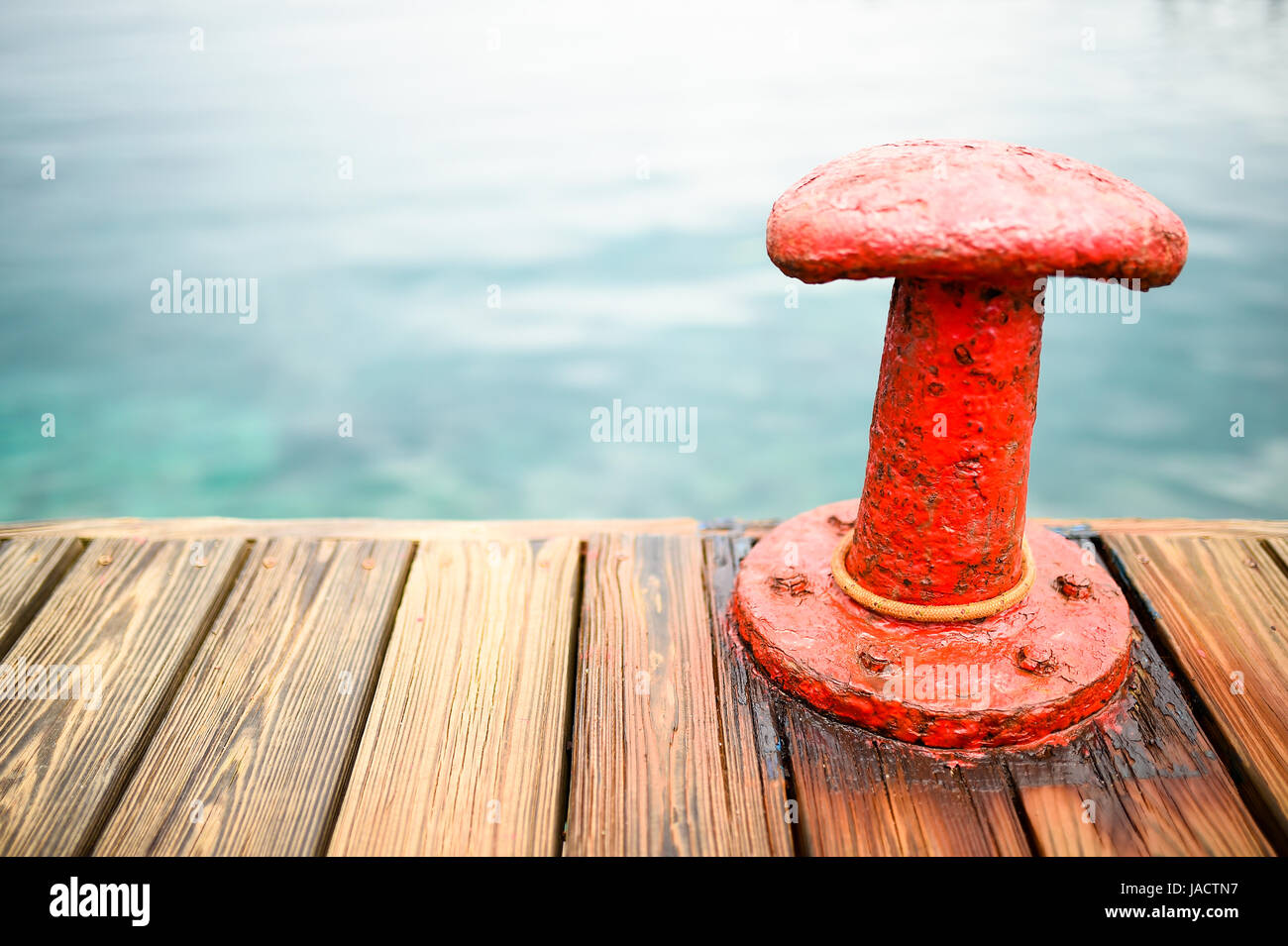 Red bollard with a mooring rope on the pier at the port and sea water ...
