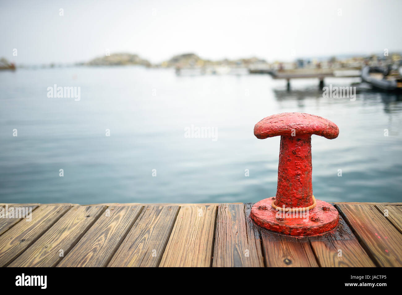 Red bollard with a mooring rope on the pier at the port and sea water ...