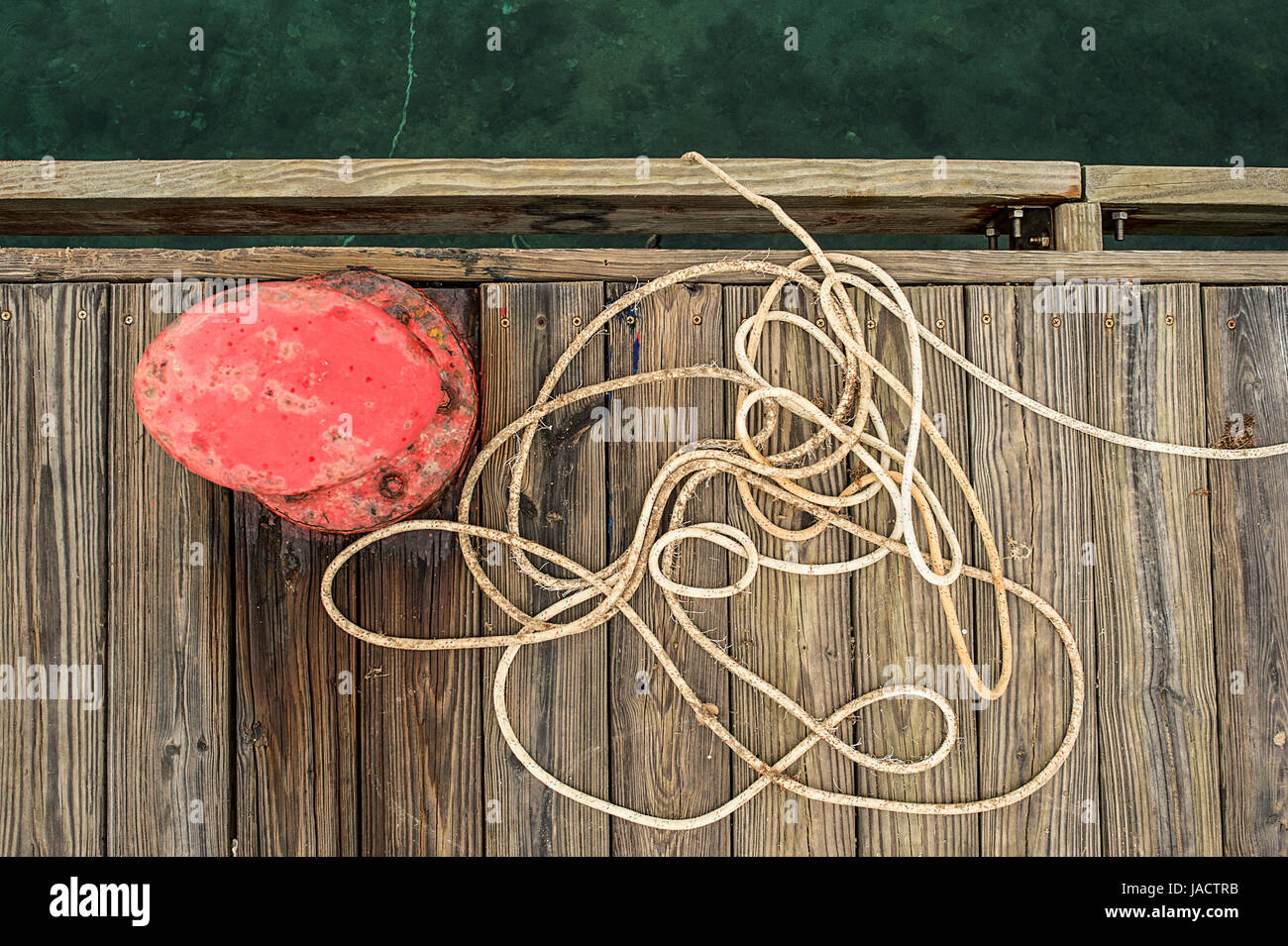 Red bollard with a mooring rope on the pier at the port and sea water ...