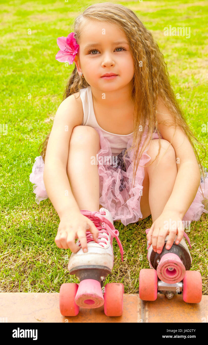 Little girl preschool beginner touching her roller skates, in a grass ...