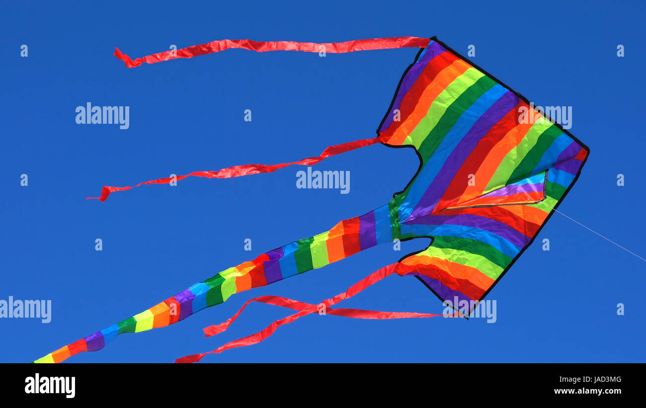Colorful rainbow kite flying against a sunny blue sky Stock Photo - Alamy