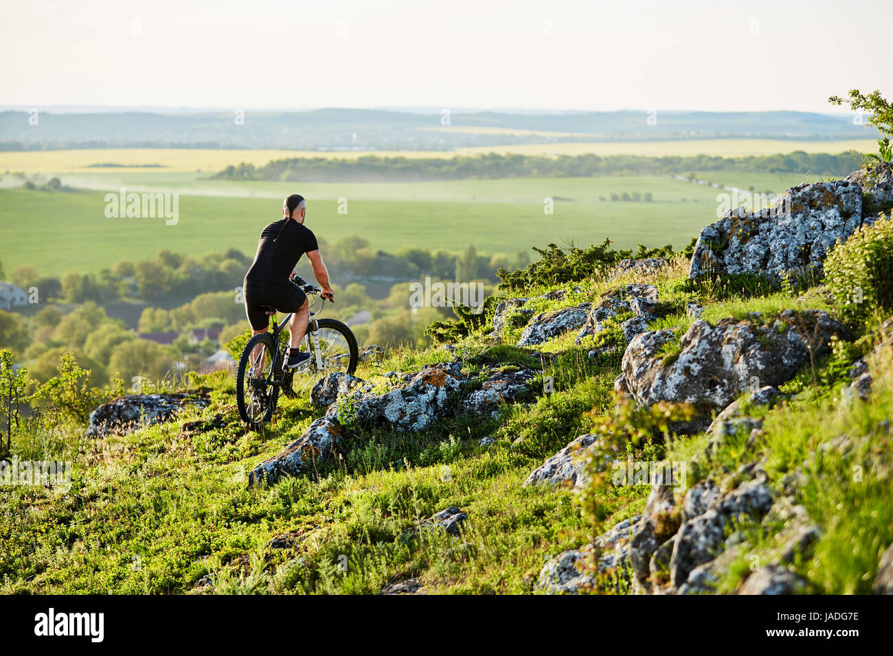 Rear view of the young cyclist riding the bike on the rocky trail in ...