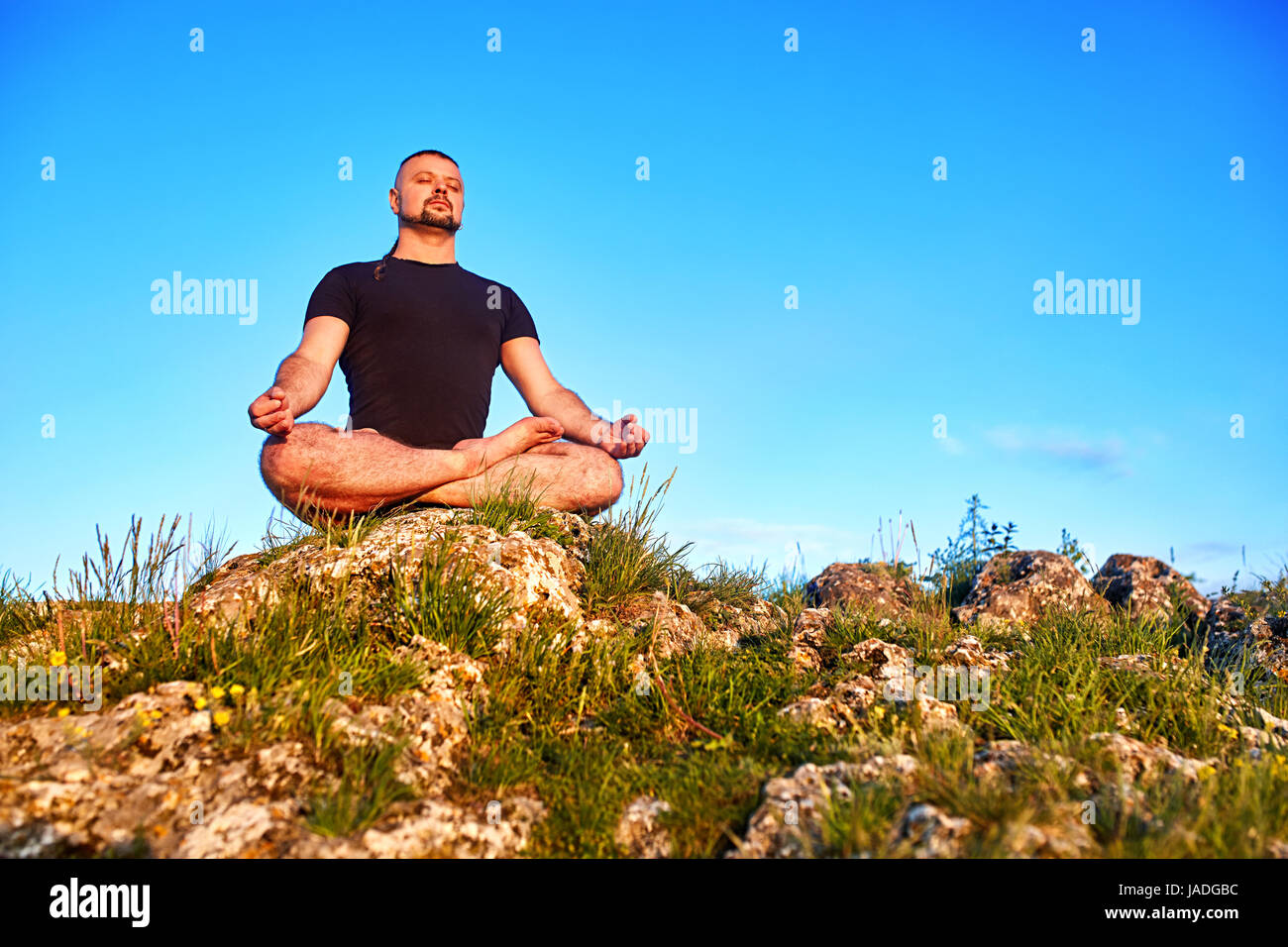Portrait of the man sitting on a rock in the lotus position against ...