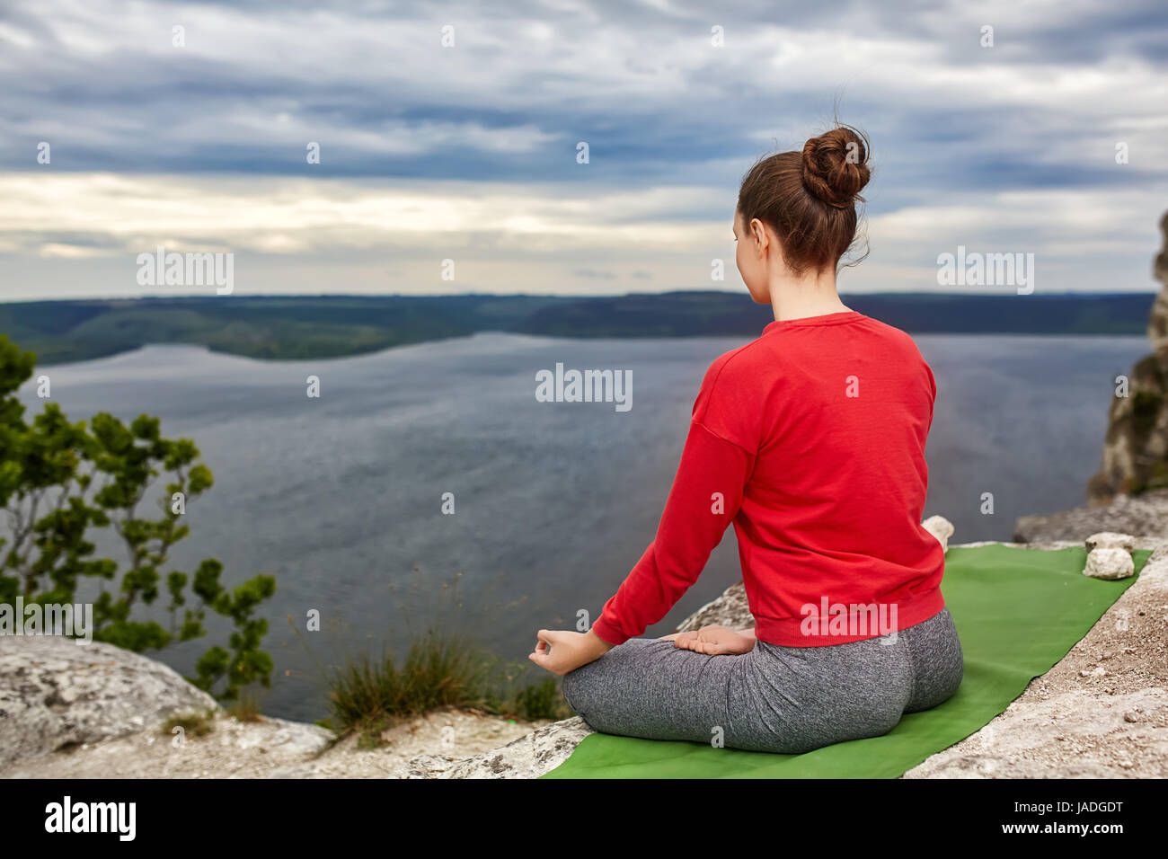 Young woman meditating in a lotus pose on the rock above big river ...