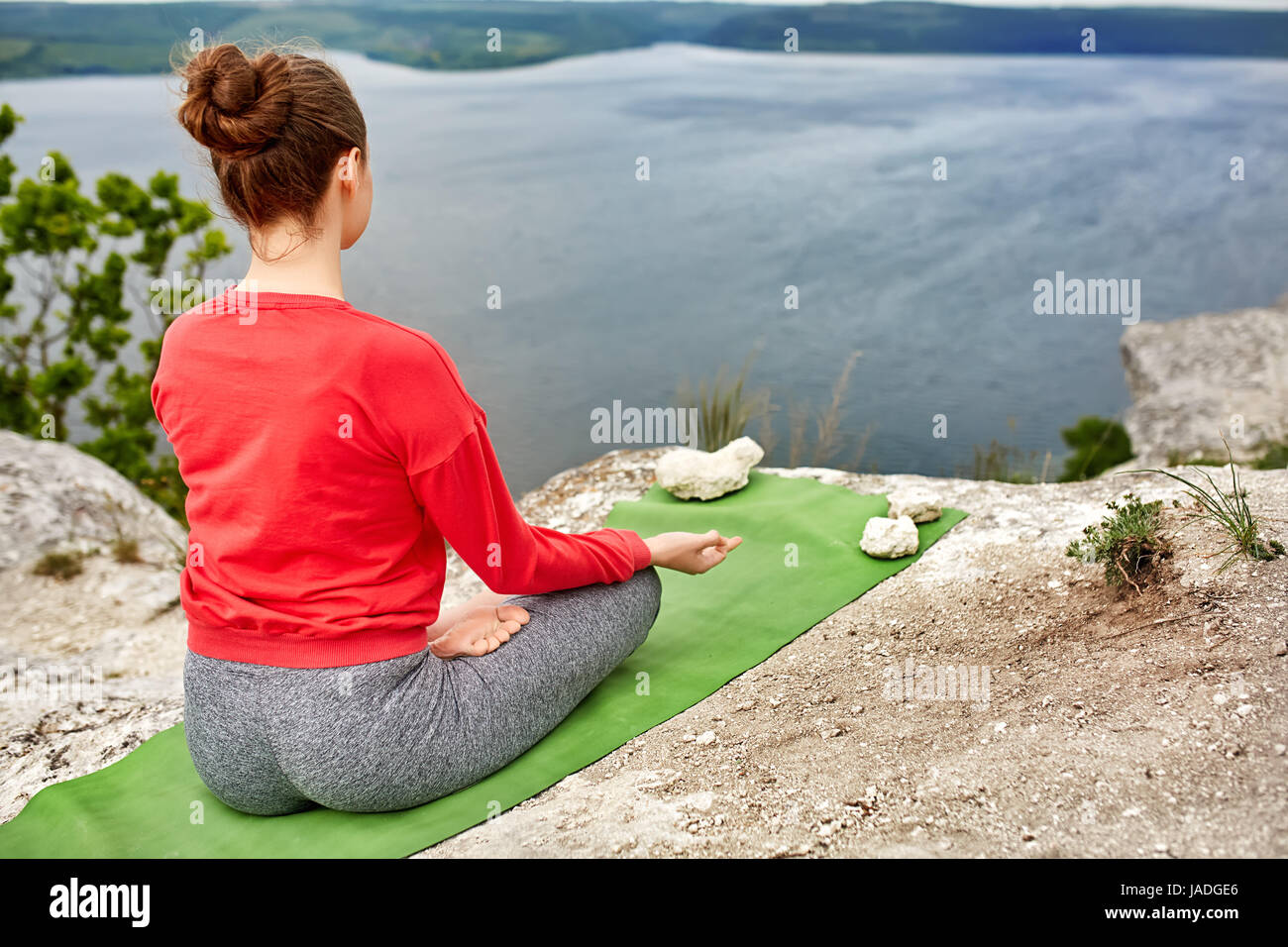 Young woman meditating in a lotus pose on the rock above big river ...