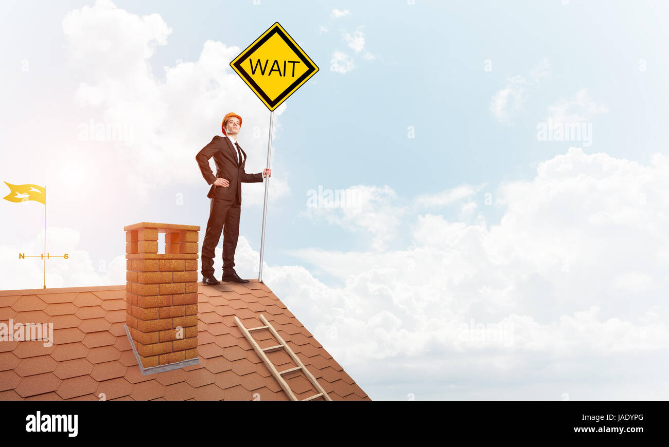 Young businessman on house brick roof holding yellow signboard. Mixed ...