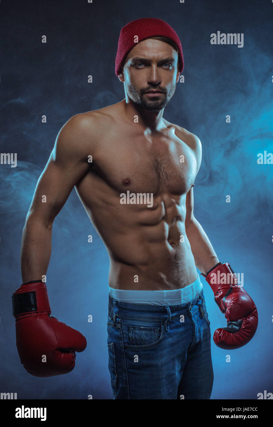Young athletic boxer exhibiting his six-pack abdominals wearing gloves ...
