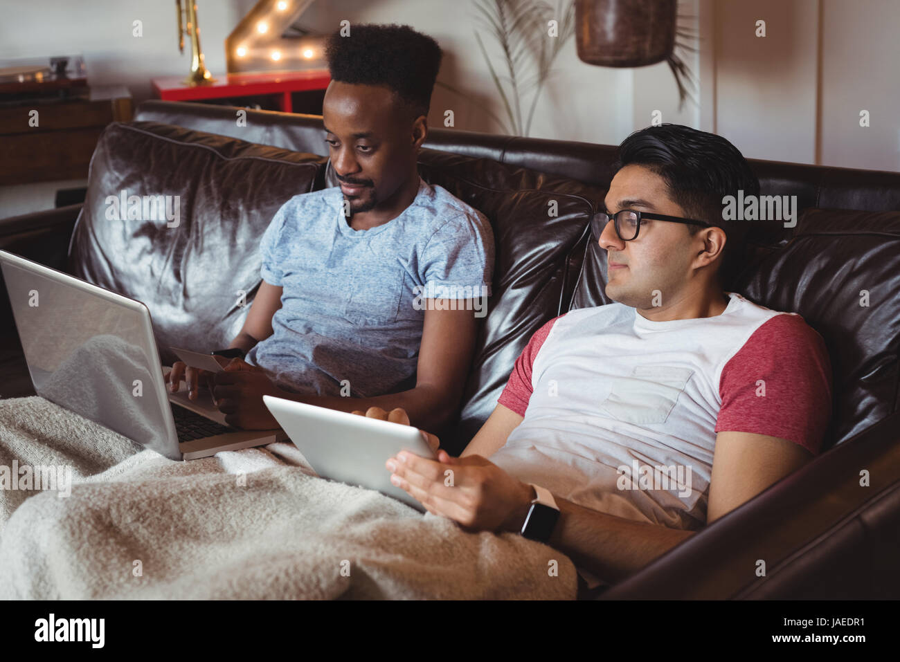 Gay couple using digital tablet and laptop while sitting on a couch at ...